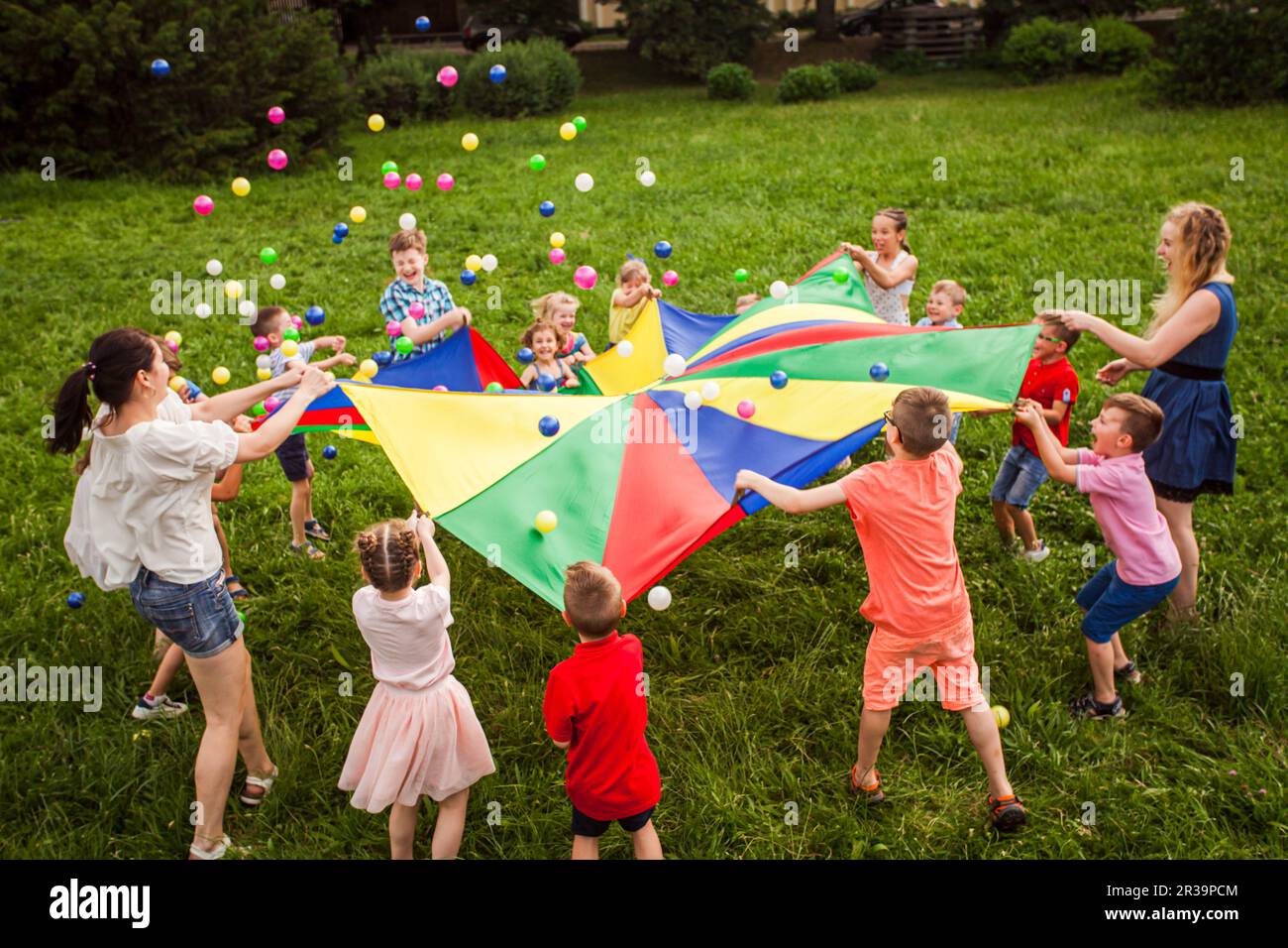 Happy kids waving rainbow parachute full of balls Stock Photo - Alamy