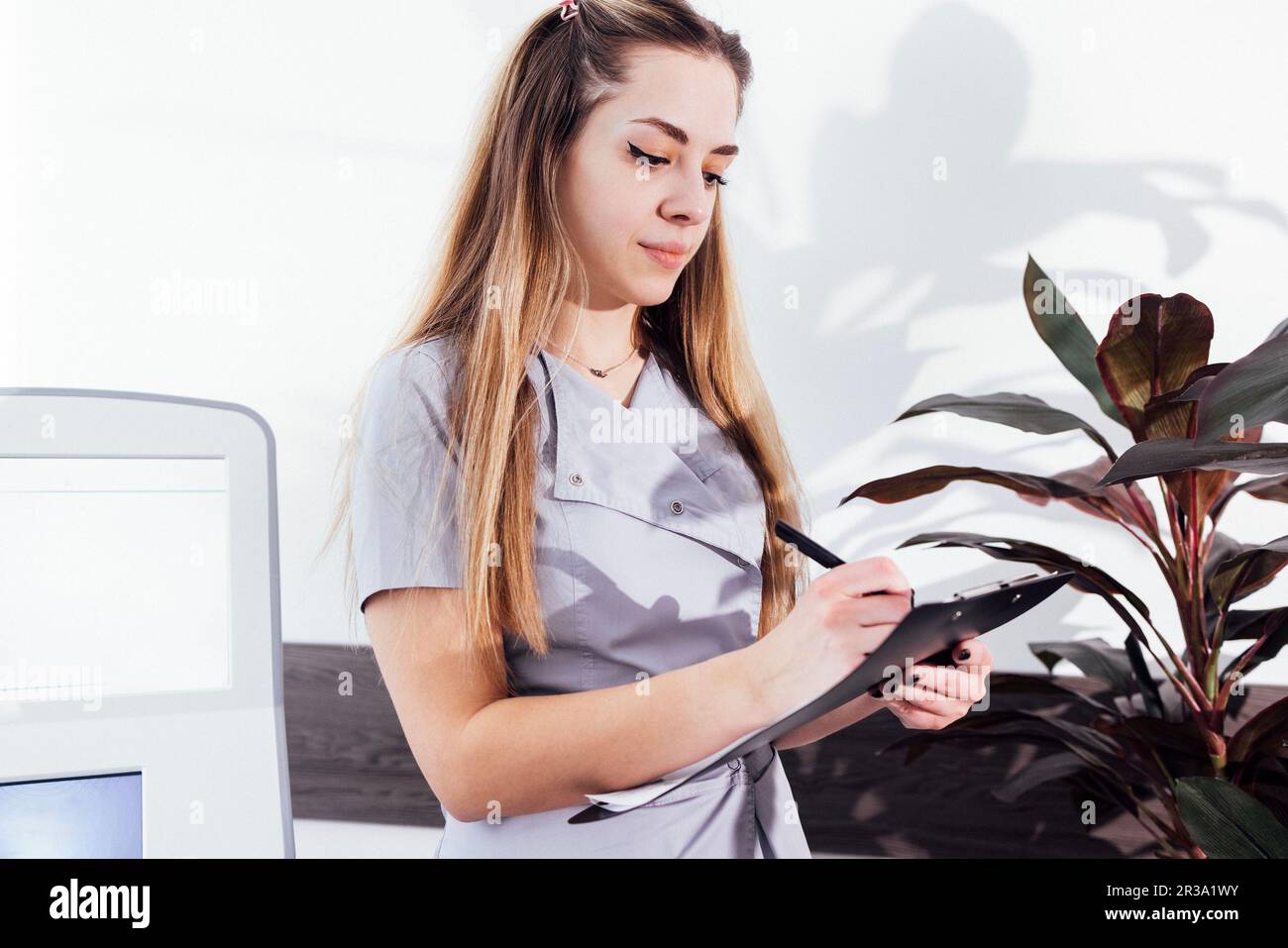 Female doctor in gray uniform writing down her patient details on paper ...