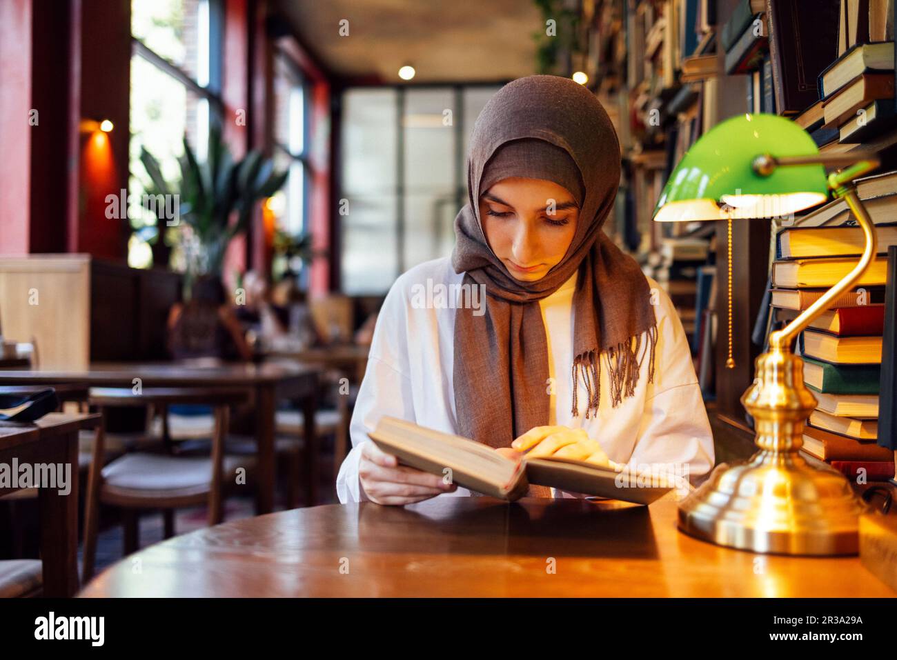 Serious Islamic teen girl in hijab reading book at library. Thoughtful ...