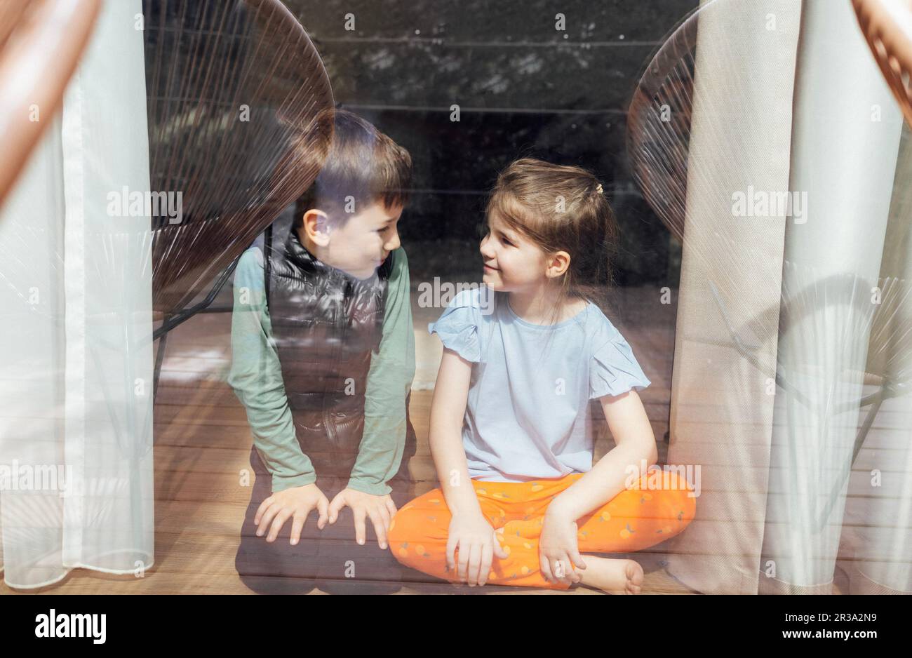 Cute kids are sitting on floor outside panoramic window. Happy boy and ...