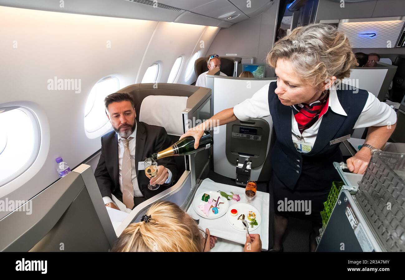 Female cabin crew pouring a glass of champaign in business class of an ...
