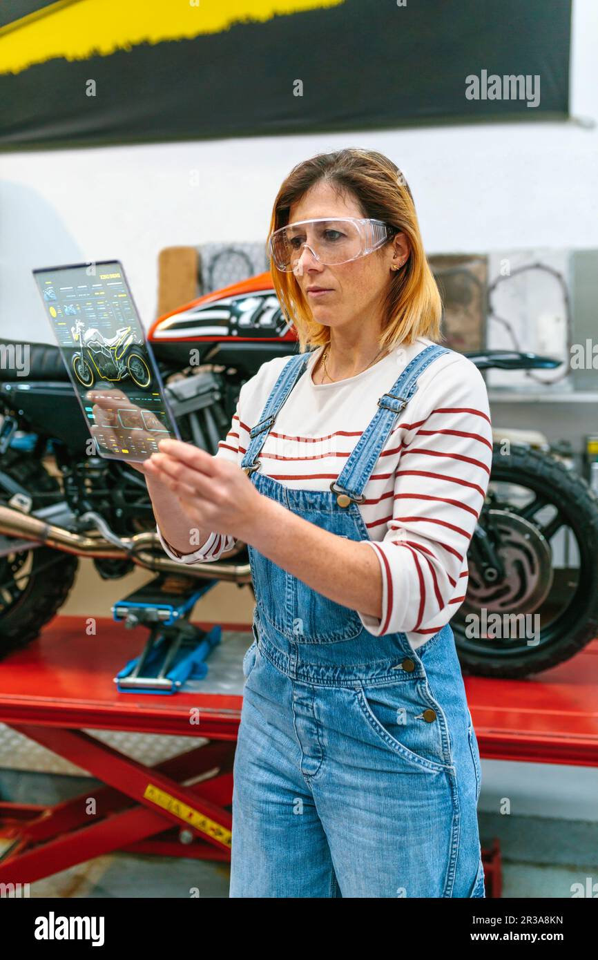 Female mechanic using transparent digital tablet with motorcycle ...