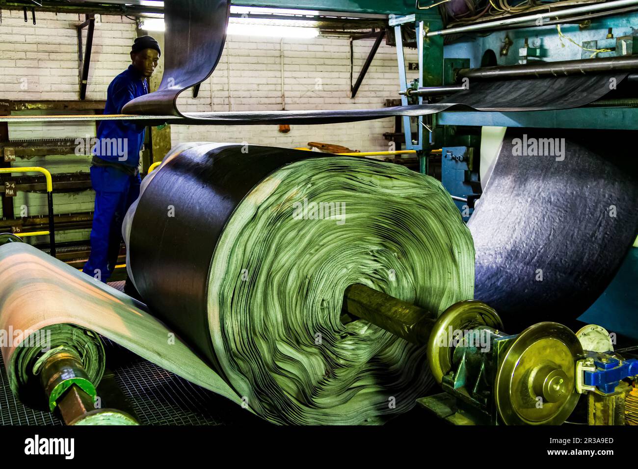 African factory worker checking a roll of rubber on a machine in a ...