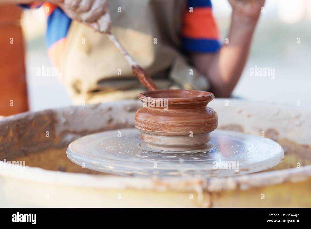 Hands of young potter, creating an earthen jar on the circle, close-up ...