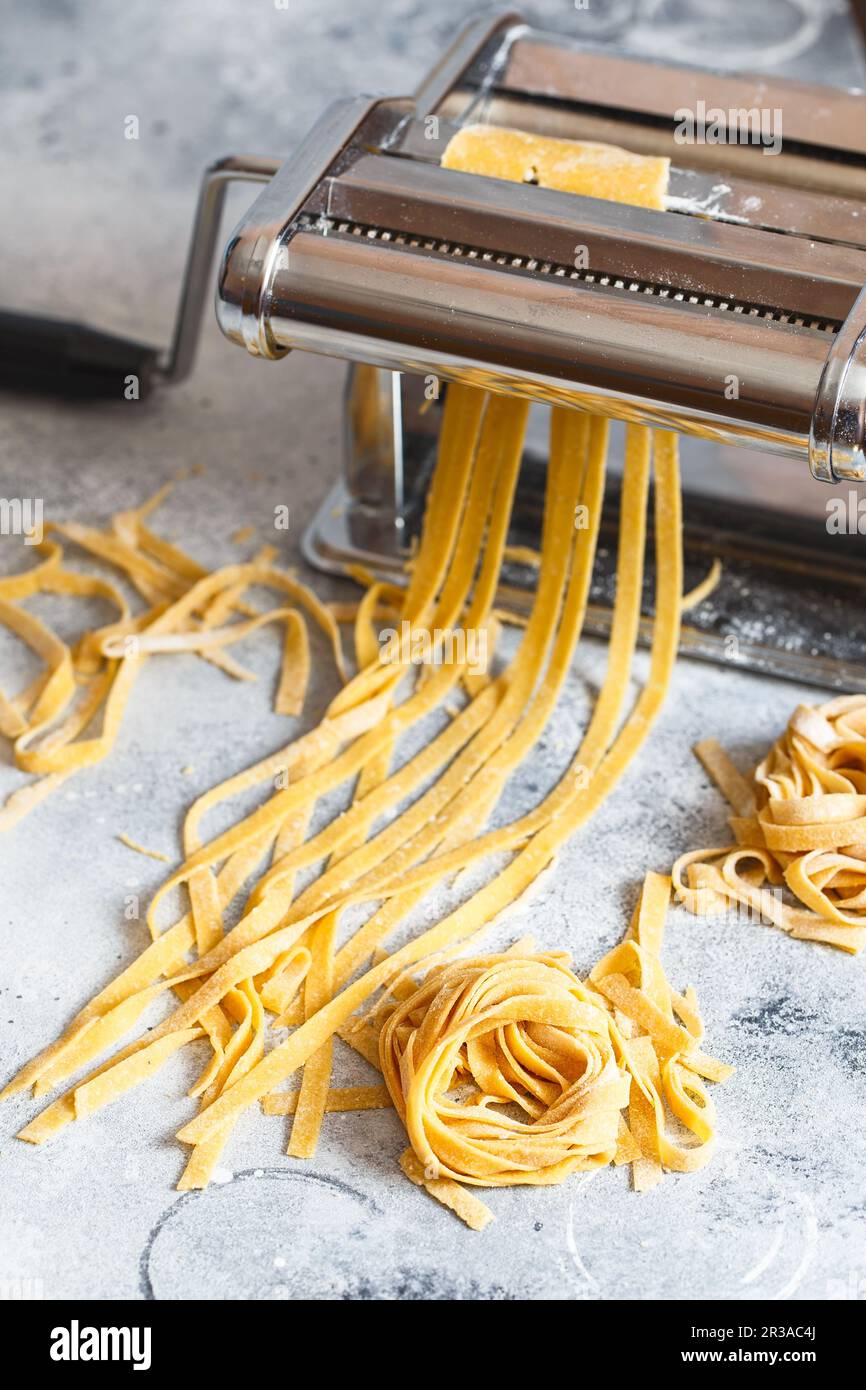 Metal pasta maker with dough. Fettuccine coming out of a manual pasta ...