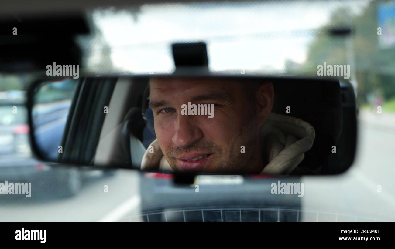 Happy young Caucasian male driving a car in city looking and winking in ...