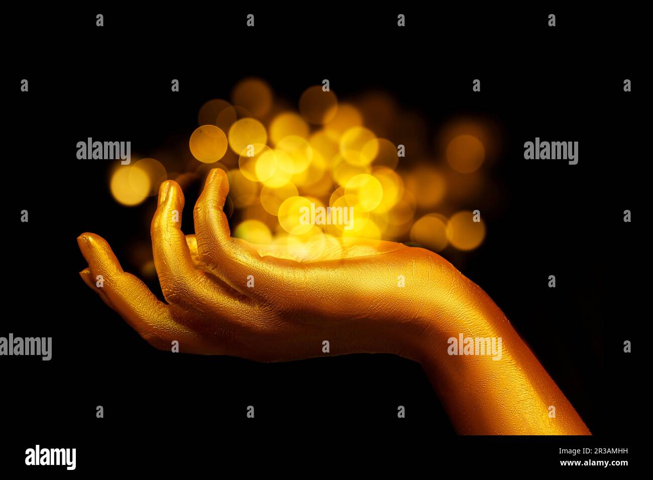 A golden female hand holds a golden bokeh on a black background ...
