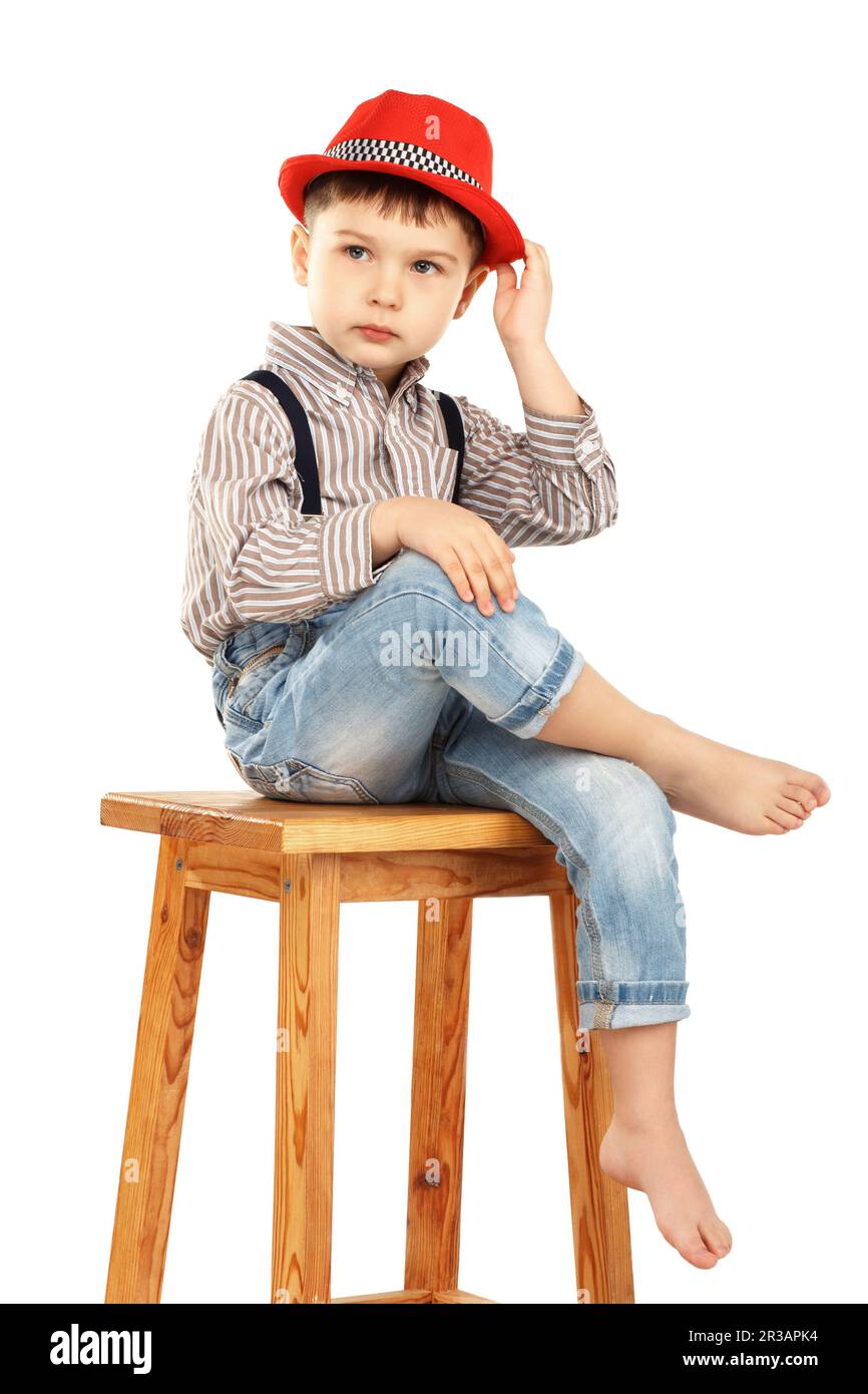 Portrait of a funny little boy sitting on a high stool in a red hat ...