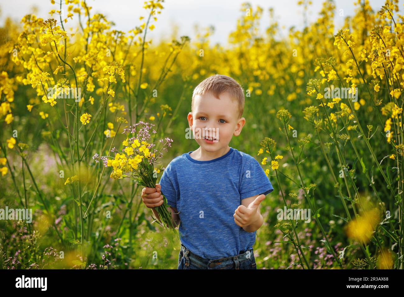 Little happy boy with a bouquet of flowers is in the yellow flowering ...