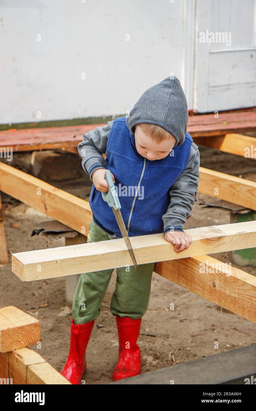 Little studious boy sawing a wooden board. Home construction. Little ...