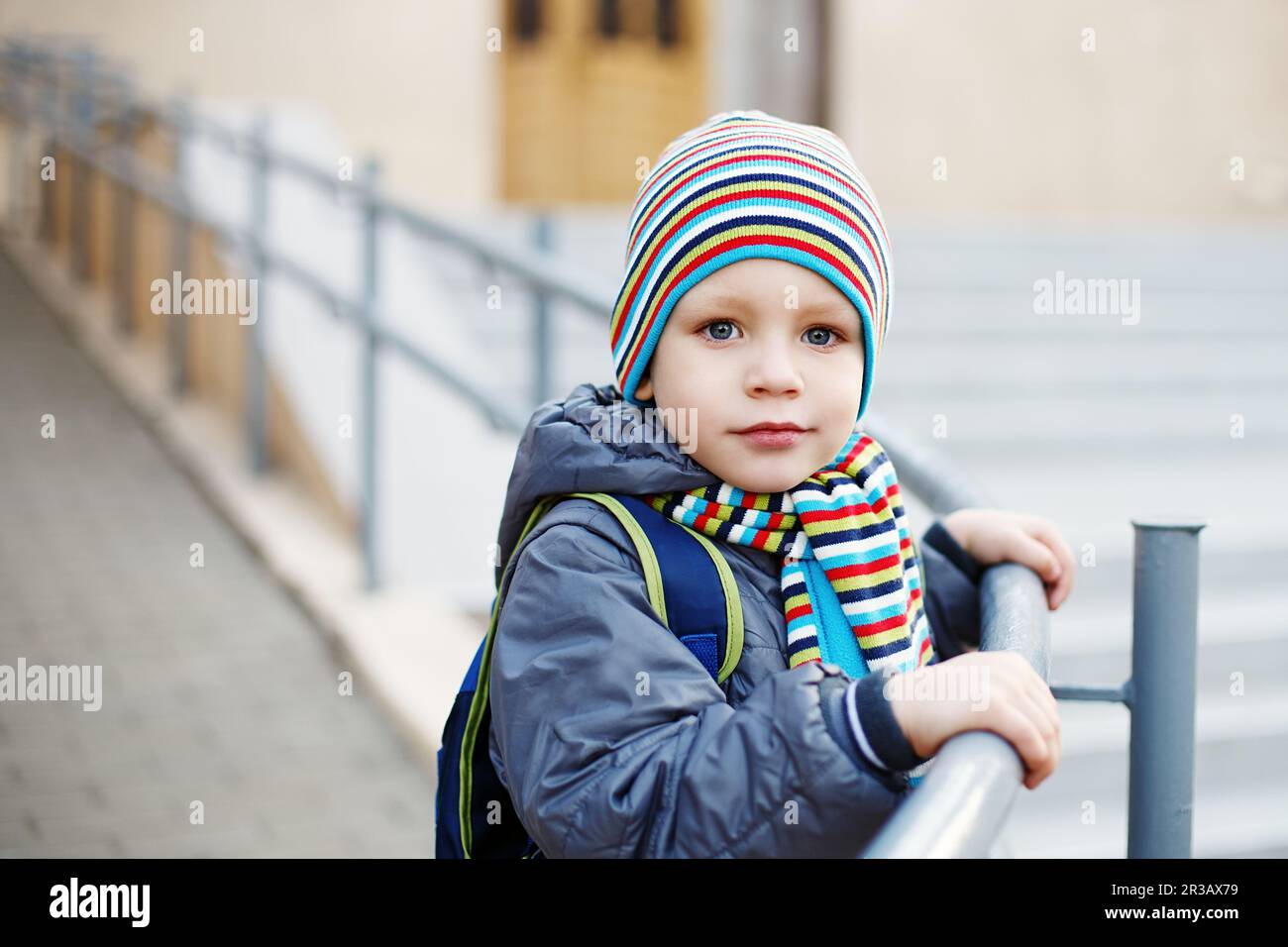 Beautiful little boy in bright striped hat and scarf near the school ...