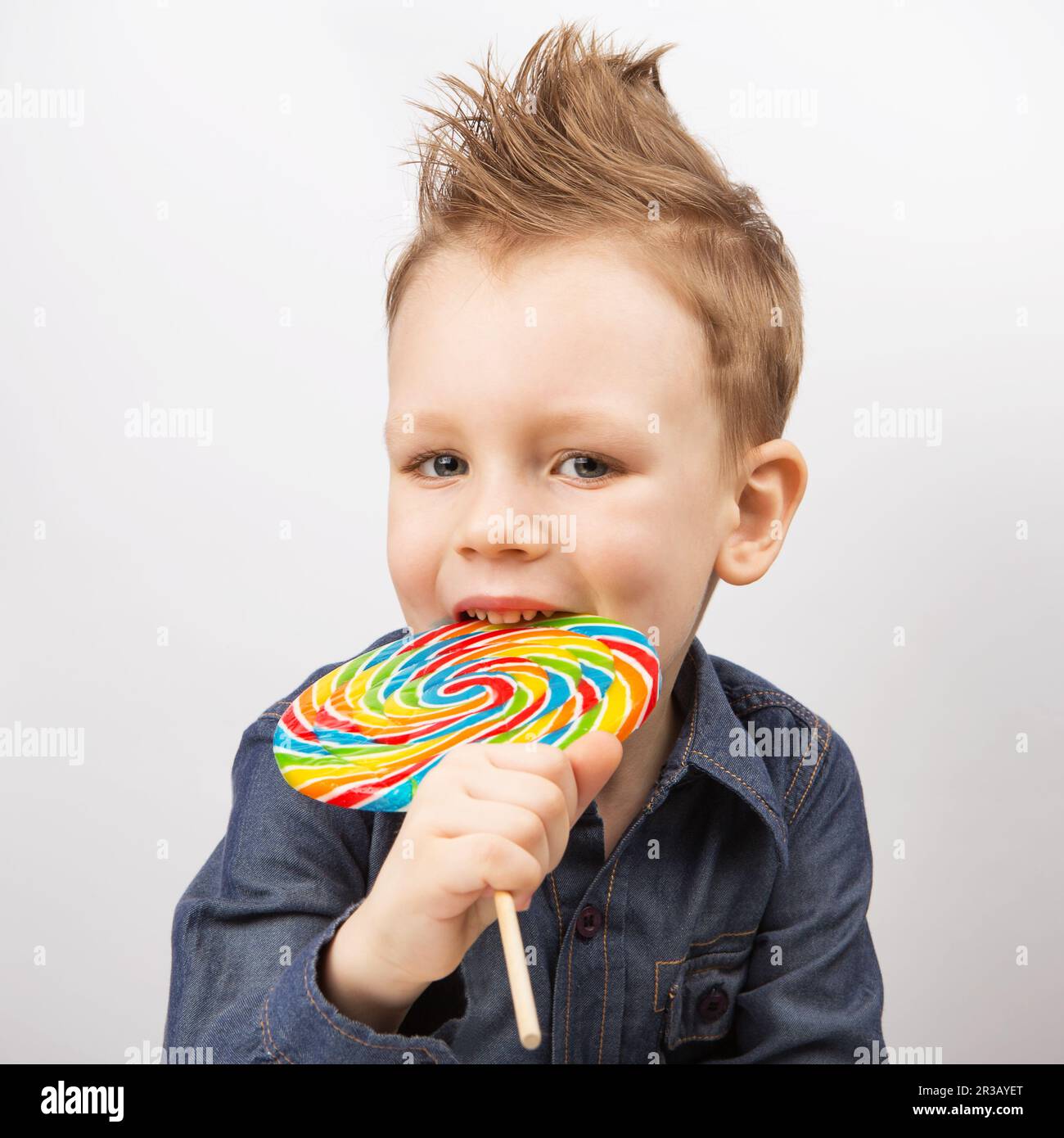A boy in a denim shirt eating lollipop. Happy kid with a big candy ...