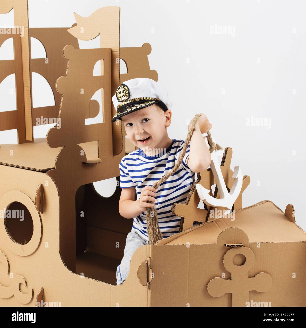 Little boy playing with cardboard ship on white background. Happy kids ...