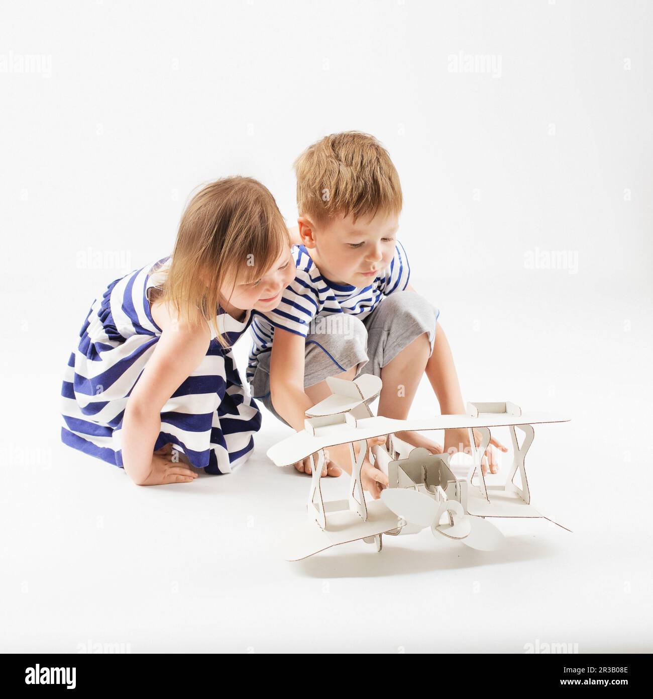 Little Children playing with paper toy airplane sitting on the floor ...