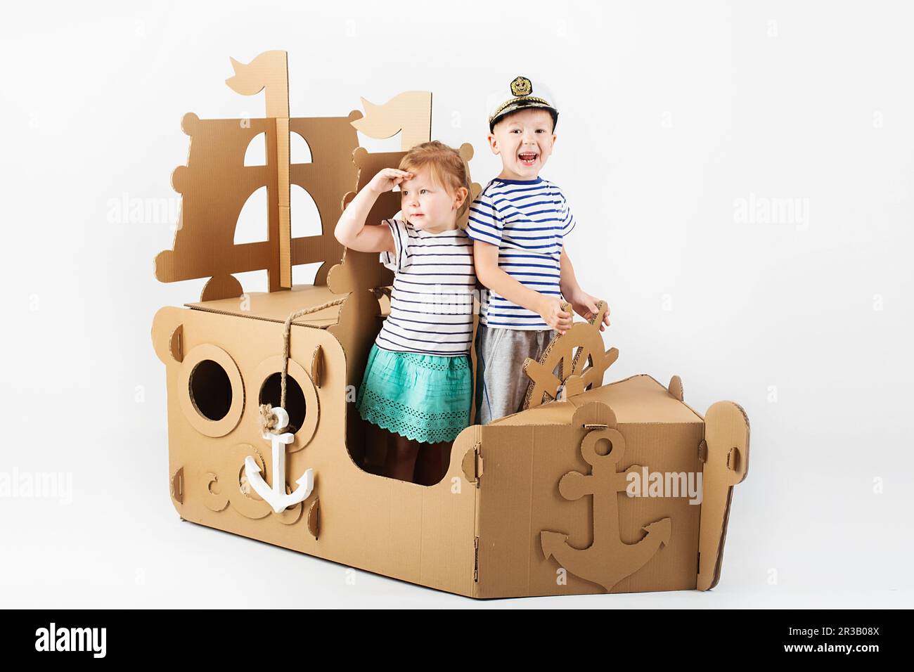 Little kids playing with cardboard ship on white background. Happy ...