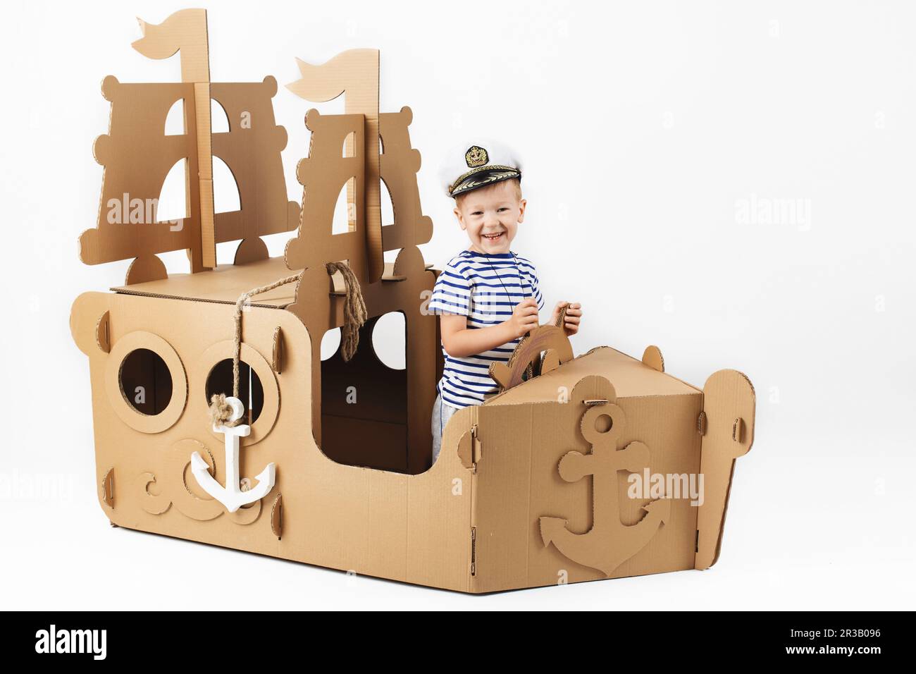 Little boy playing with cardboard ship on white background. Happy kids ...