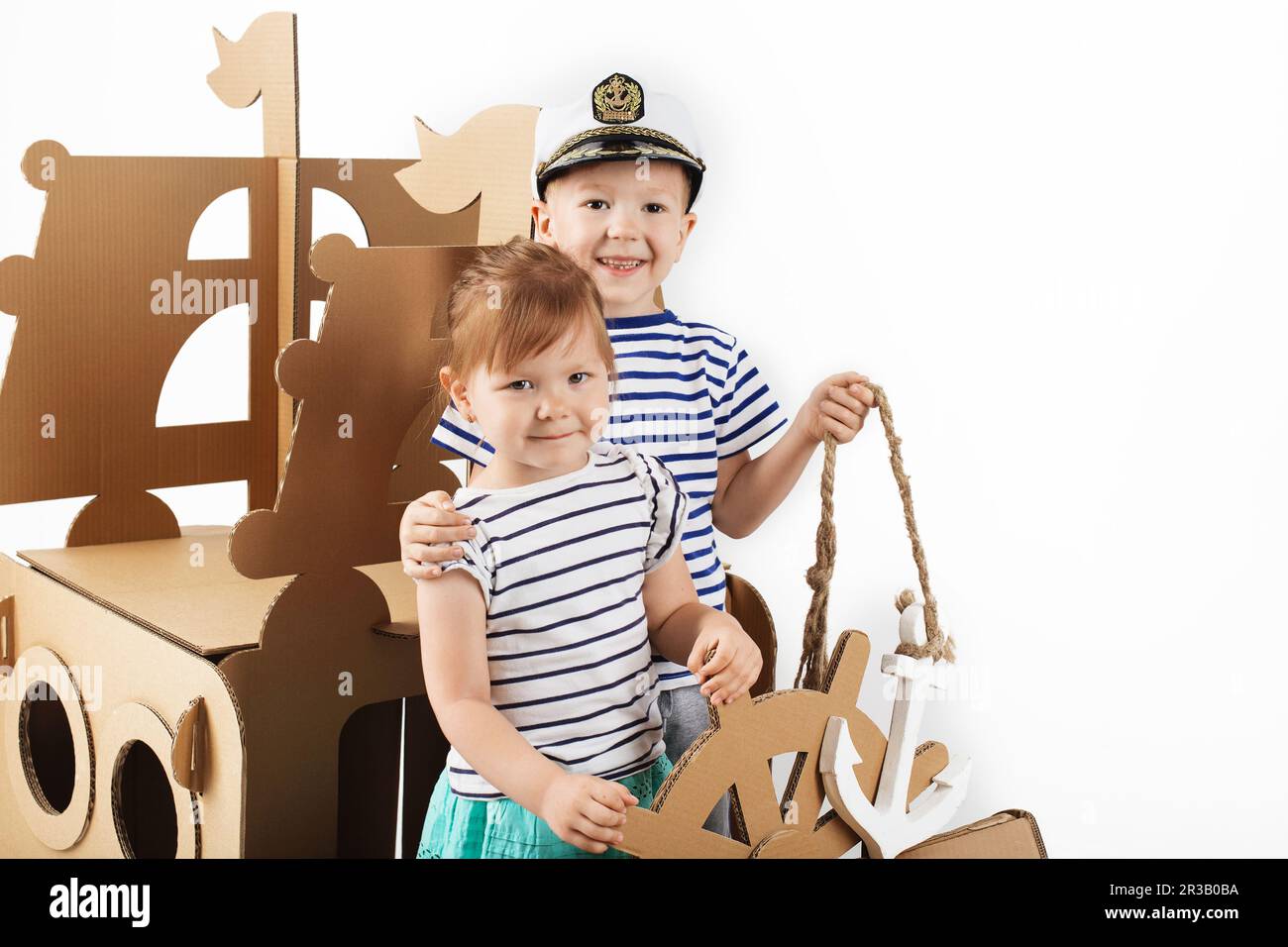 Little kids playing with cardboard ship on white background. Happy ...
