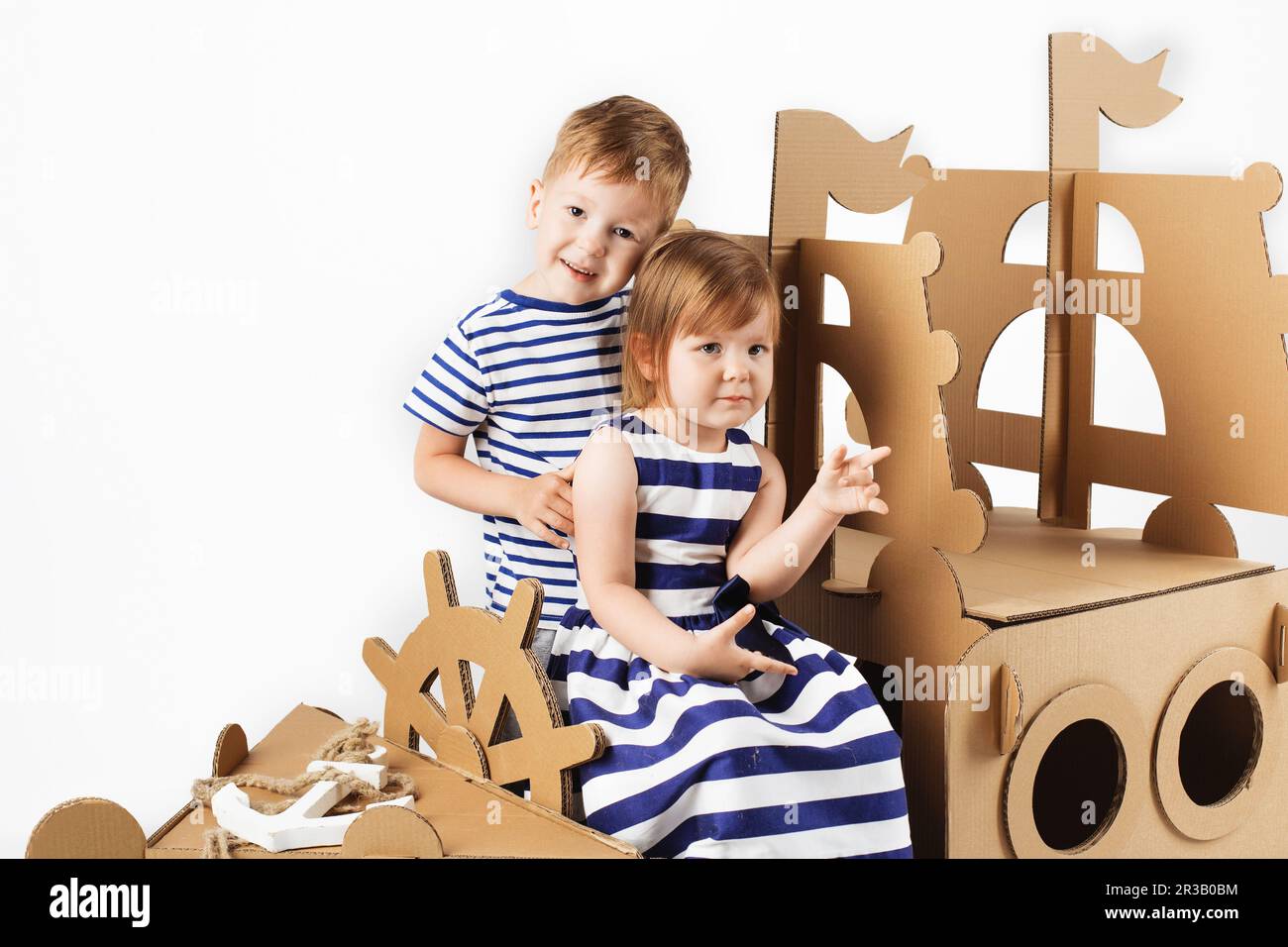 Little kids playing with cardboard ship on white background. Happy ...