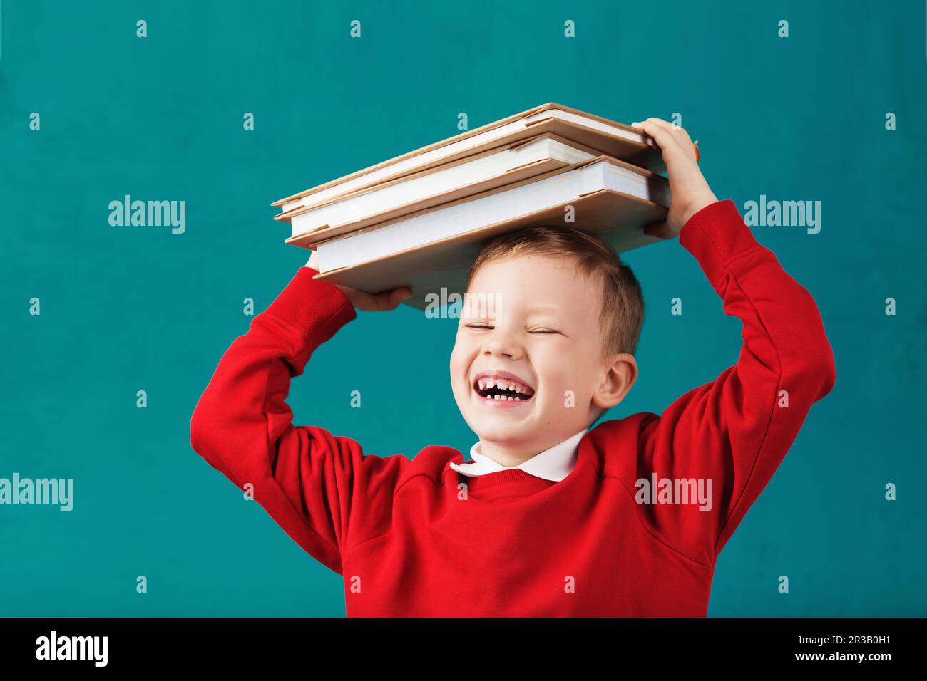 Cheerful smiling little school boy with big heavy books on his head ...