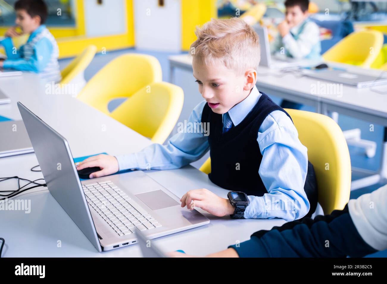 Boy with blond hair using laptop sitting in computer class Stock Photo ...