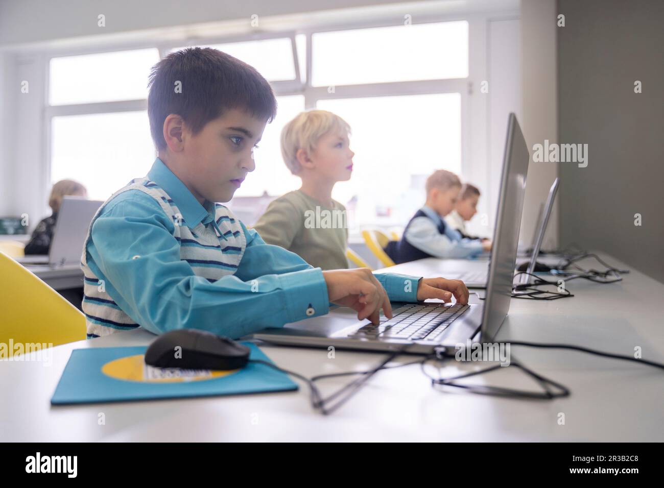 Boy doing E-learning through laptop sitting at desk in school Stock ...