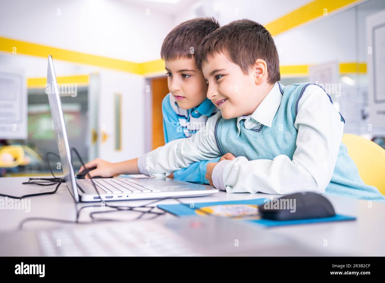 Smiling boy sharing laptop with friend at computer class in school ...
