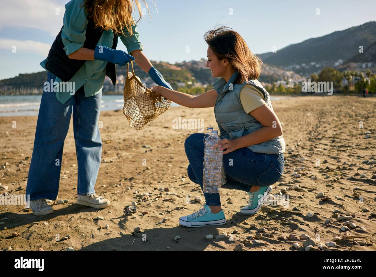 Woman putting plastic bottle in mesh bag held by volunteer at beach ...