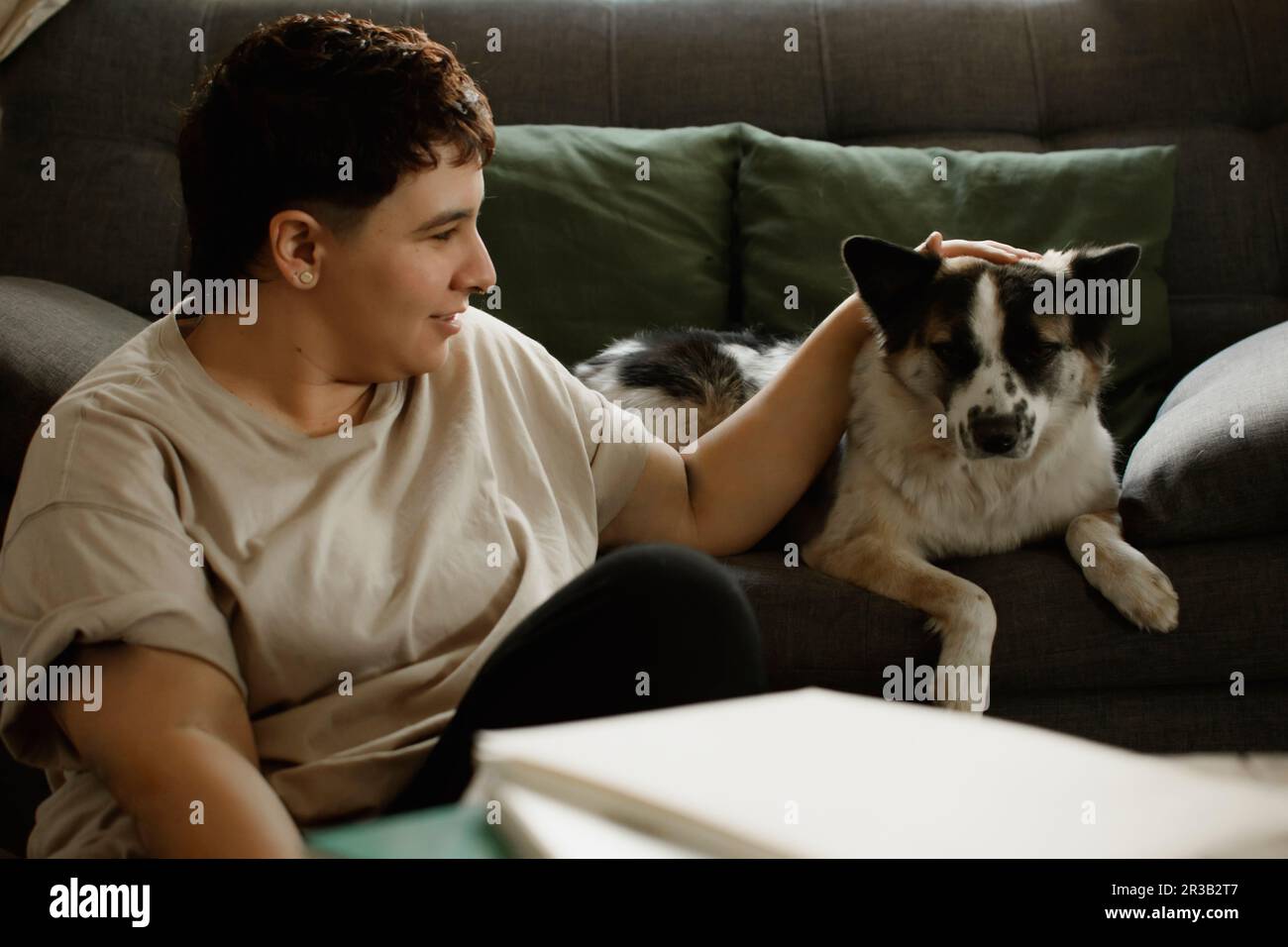 Non-binary person stroking dog sitting on sofa at home Stock Photo - Alamy
