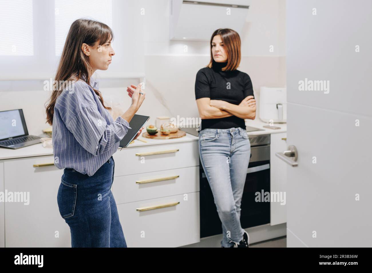 Nutritionist explaining client standing with arms crossed in kitchen at ...