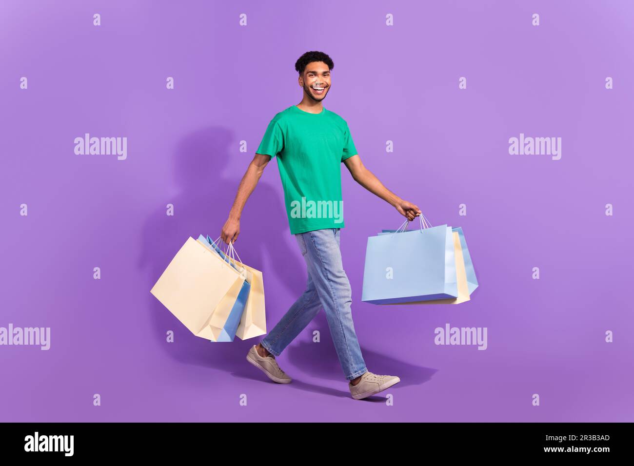 Full body length cadre of young man walking with shopping packages bags ...
