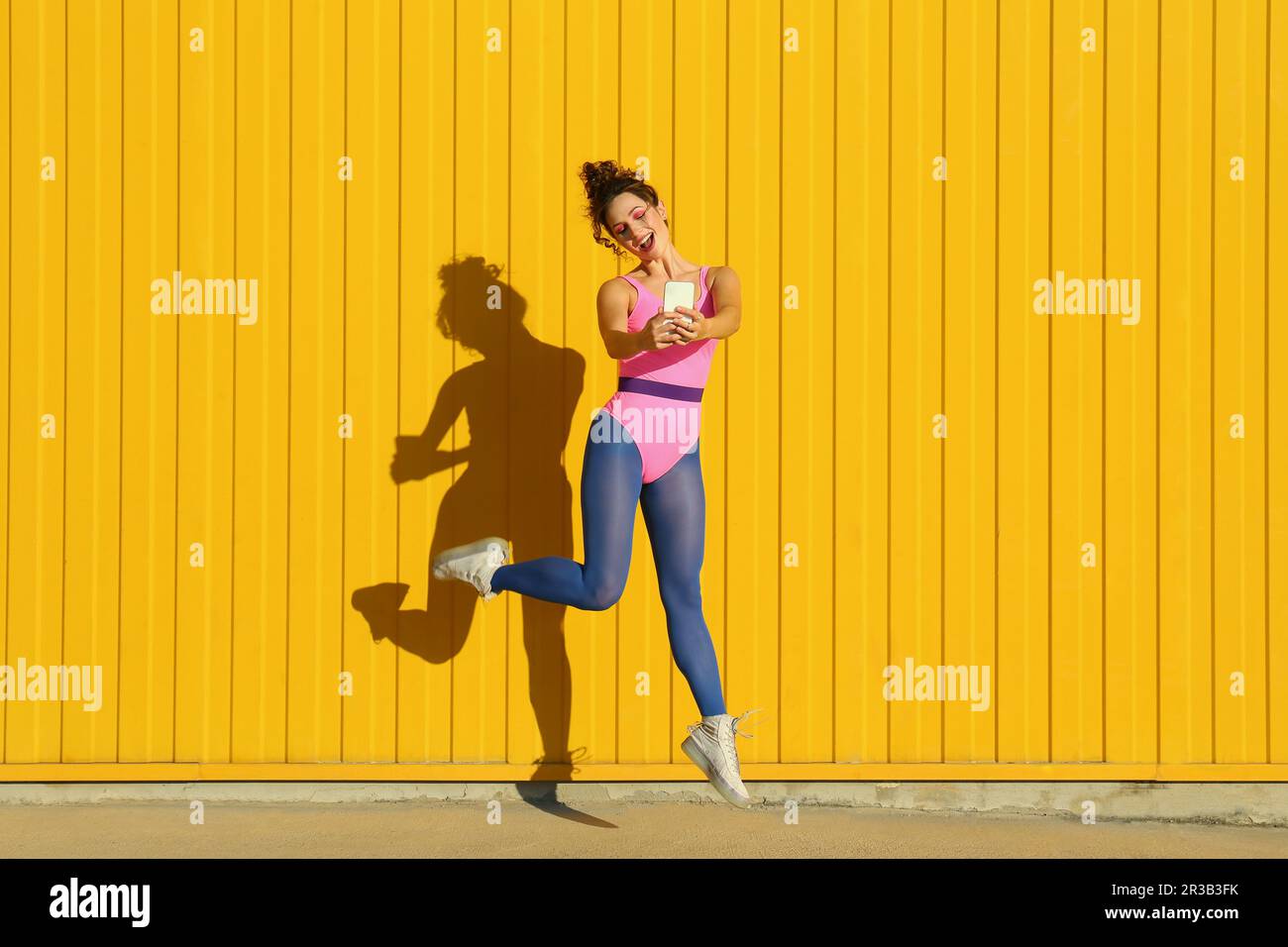 Happy woman dancing and taking selfie through smart phone in front of ...