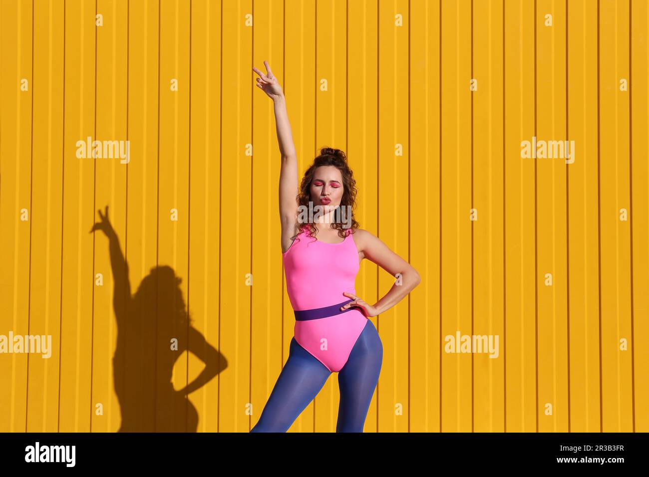 Young woman with hand on hip showing peace sign standing in front of ...