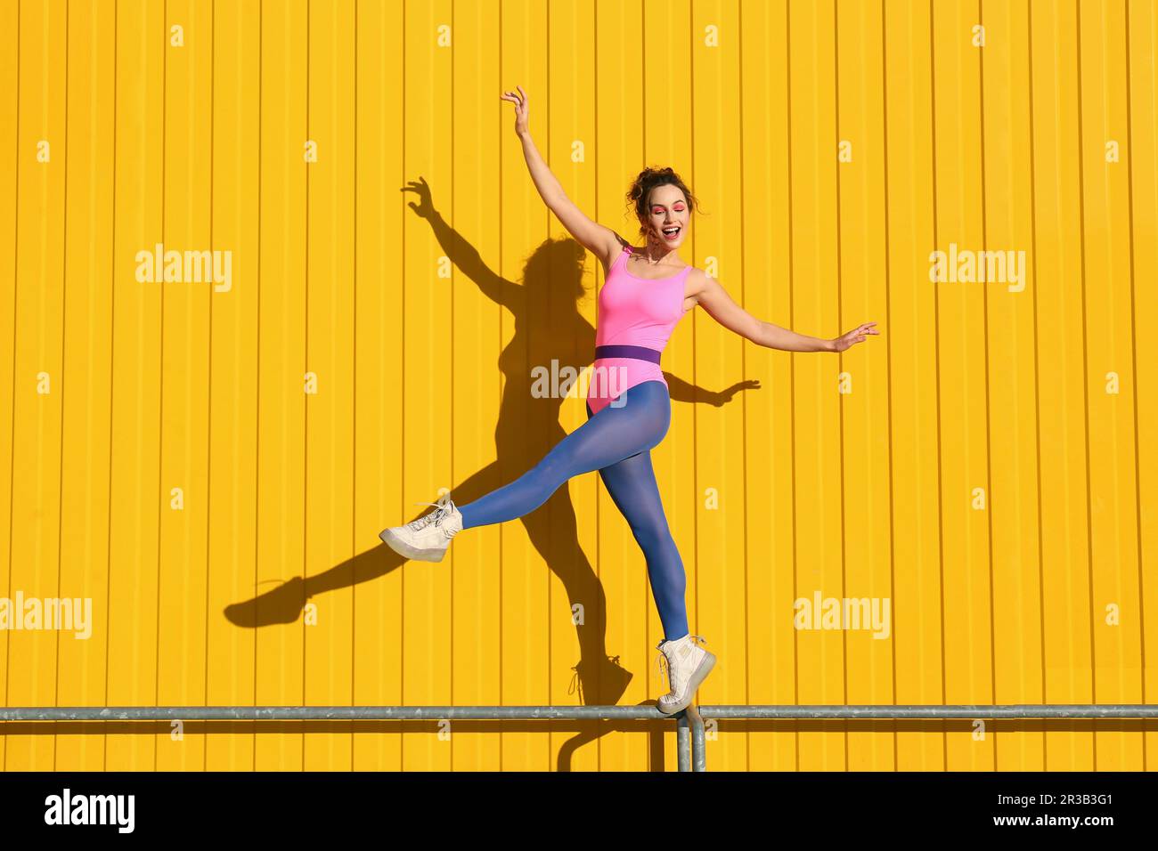 Happy woman doing ballet on railing in front of yellow wall Stock Photo ...