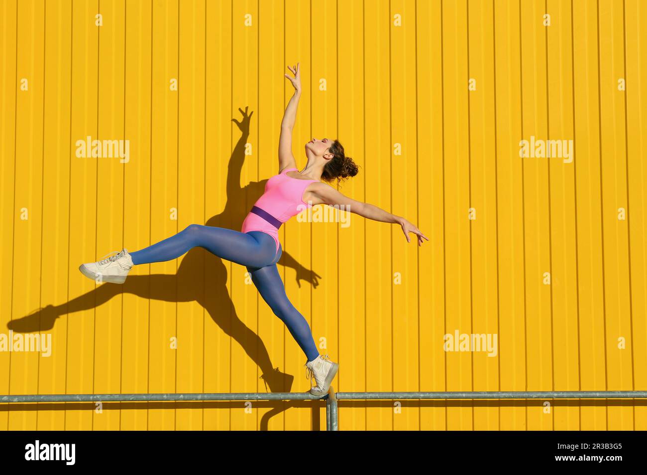 Carefree woman practicing ballet on railing in front of yellow wall ...
