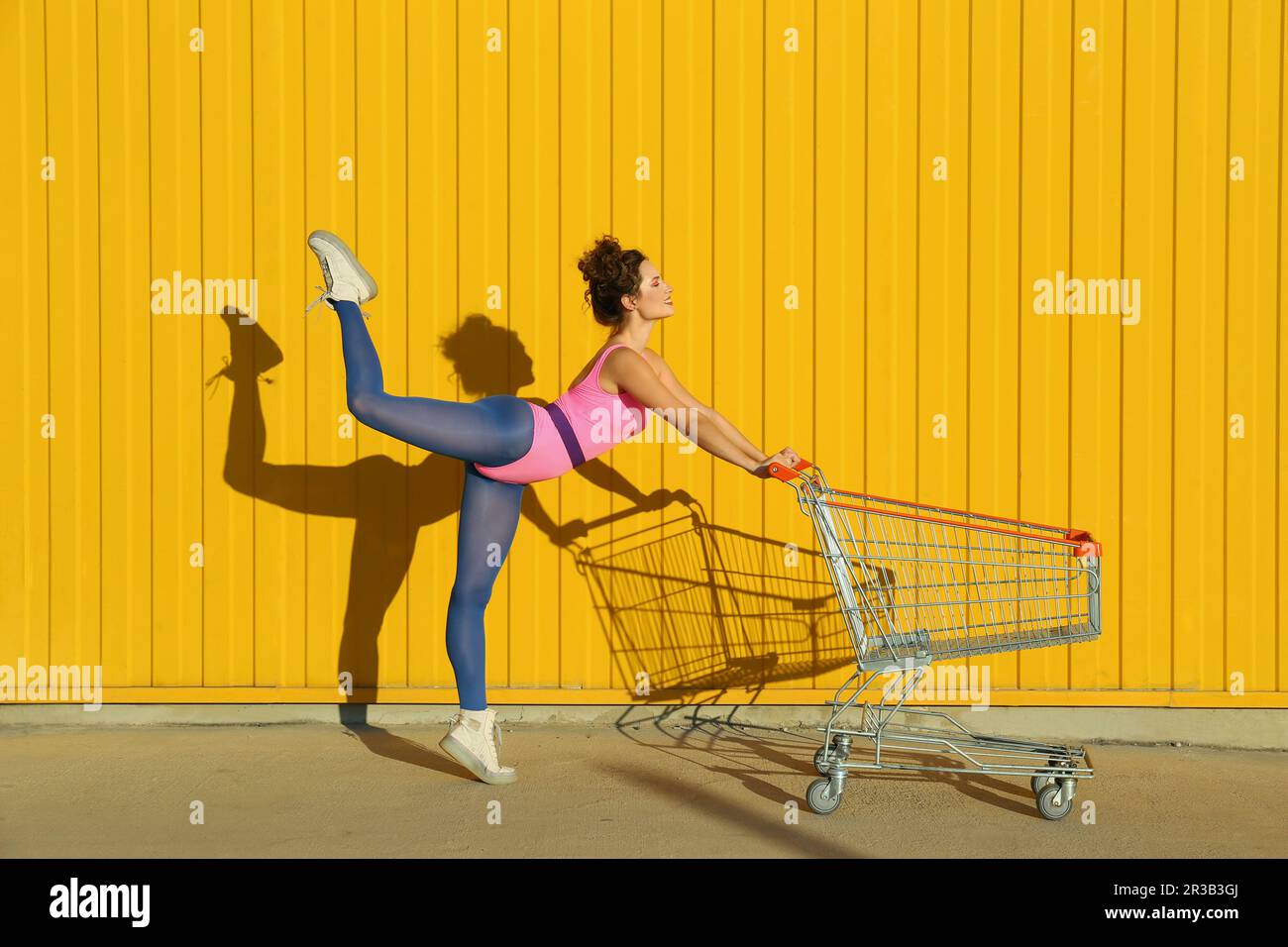 Ballet dancer pushing shopping cart in front of yellow wall Stock Photo ...