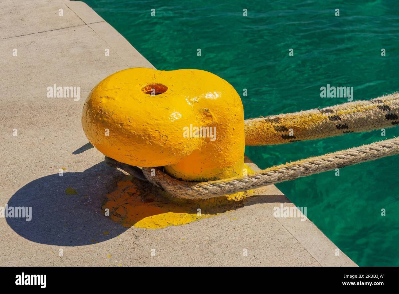 A thick hawser rope used to moor a ship on a yellow pier at the seaport ...