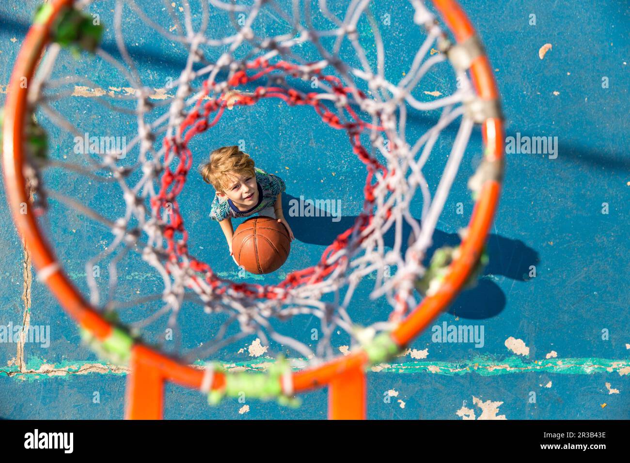 Boy standing with basketball under hoop at sports court Stock Photo - Alamy