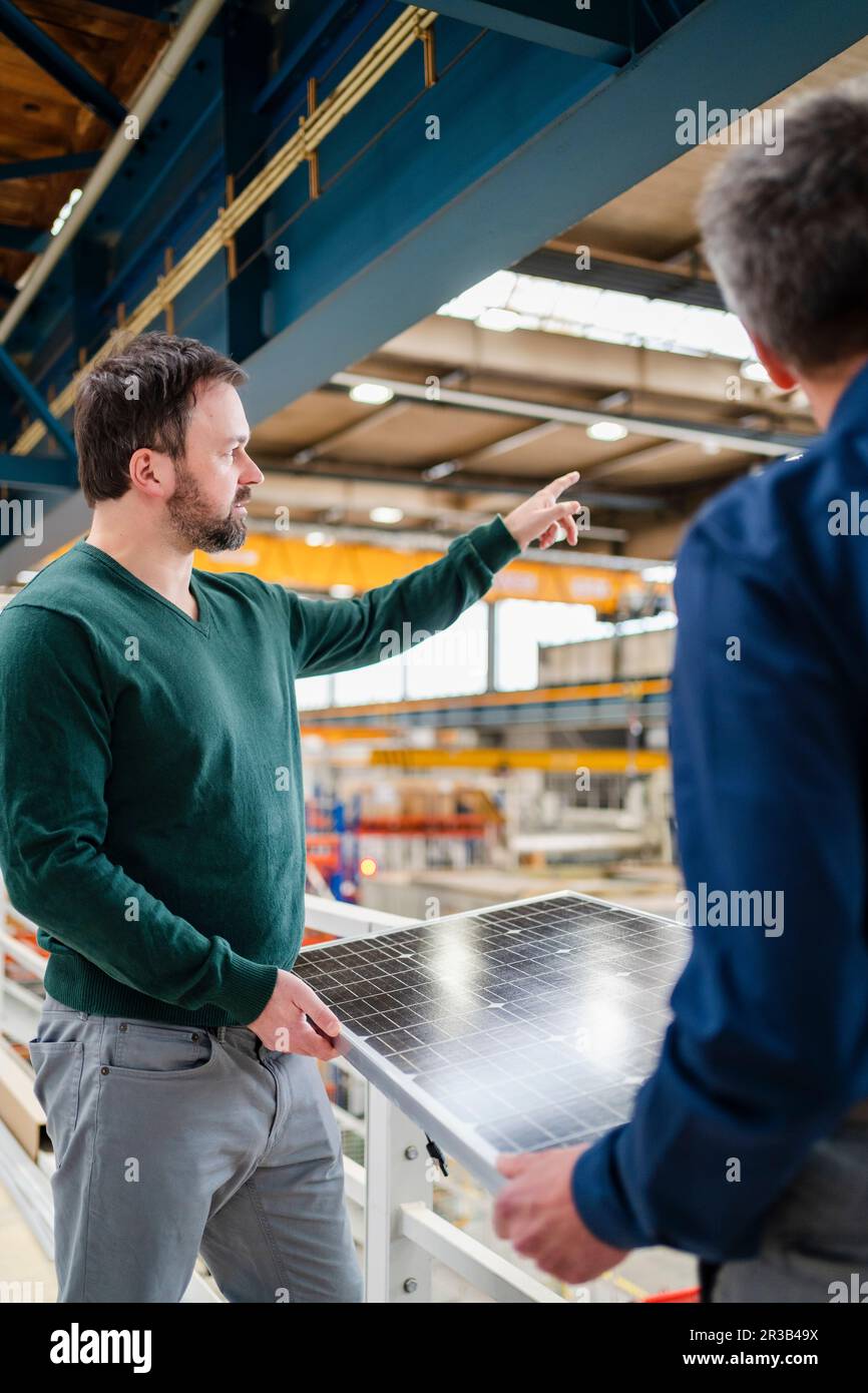 Manager pointing by businessman holding solar panel at factory Stock ...