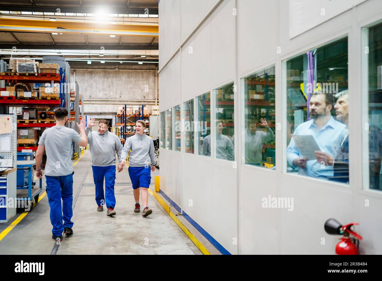 Happy colleagues giving high-five walking in production hall at factory ...