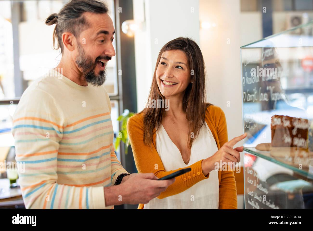 Smiling woman pointing at food display by man in coffee shop Stock ...