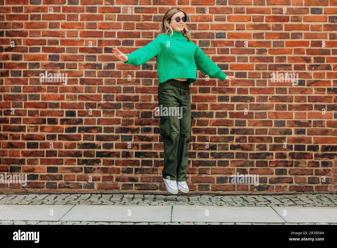 Teenage girl jumping in front of brick wall Stock Photo - Alamy
