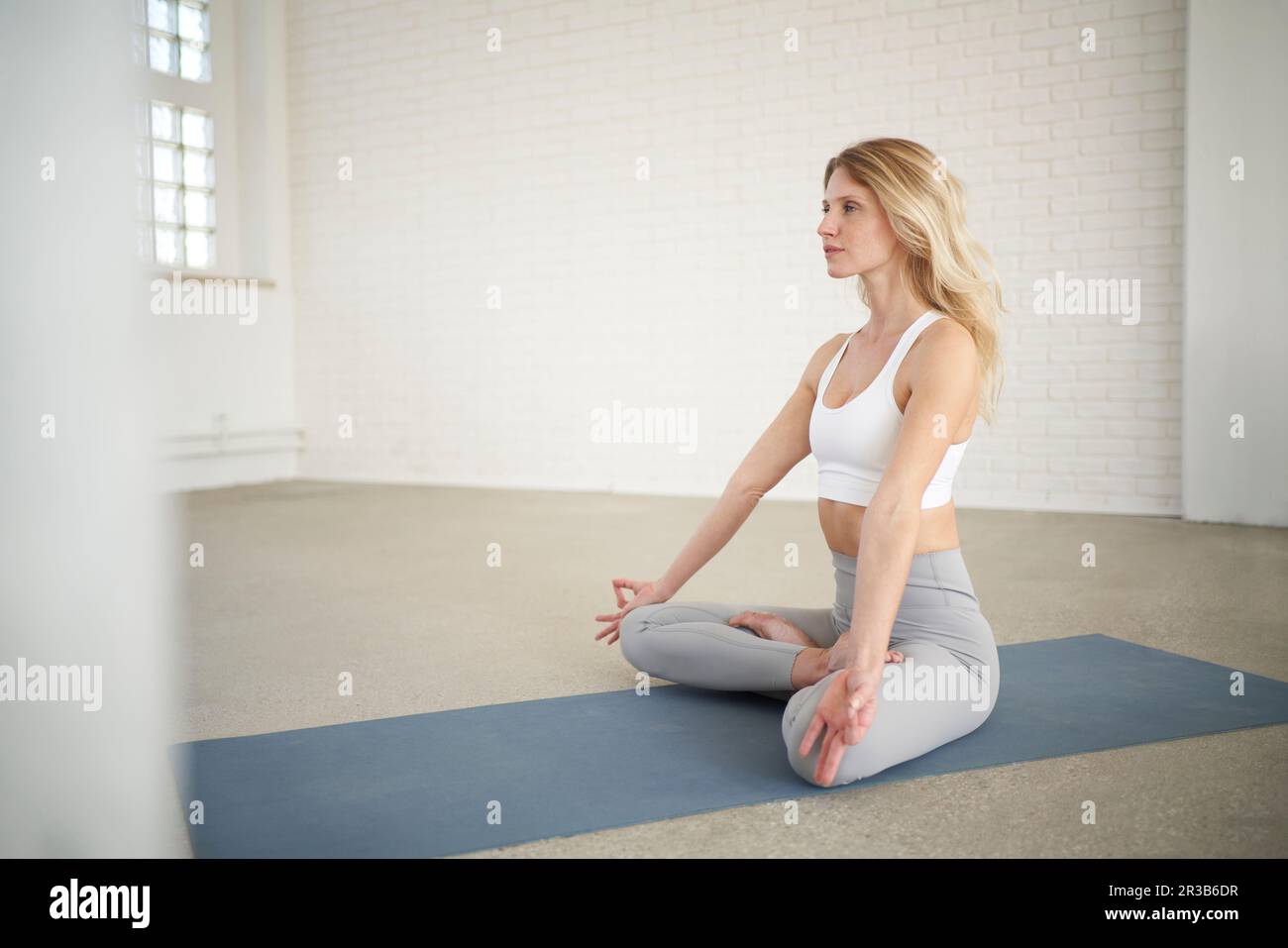 Young woman sitting cross-legged and practicing yoga in studio Stock ...