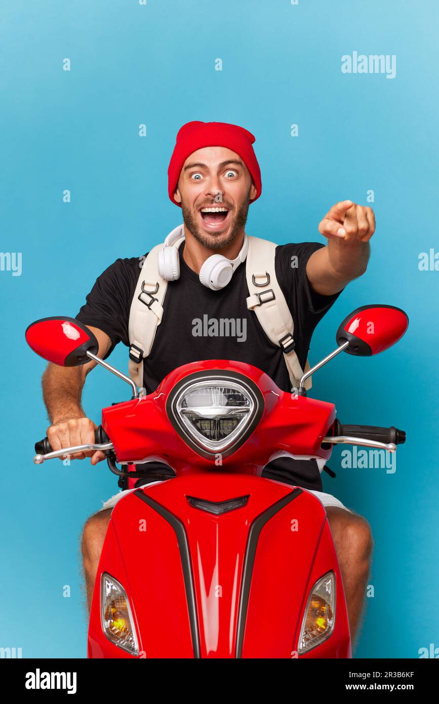 Bearded young man in red hat and black t-shirt rides red motor bike ...