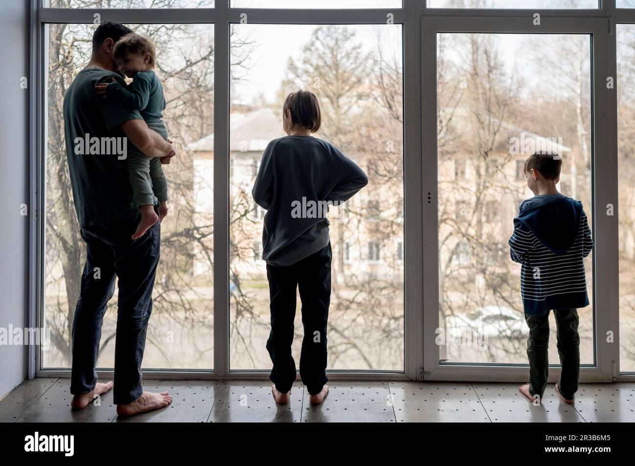 Father and sons looking out of window at home Stock Photo - Alamy