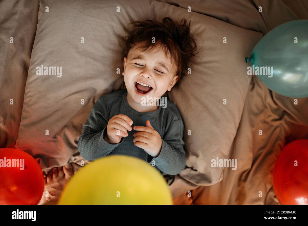 Boy laughing amidst balloons on bed Stock Photo - Alamy
