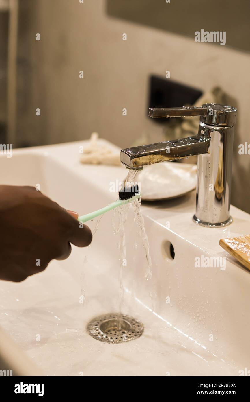 African american male hand holding toothbrush with toothpaste applied on it in bathroom. Close ...