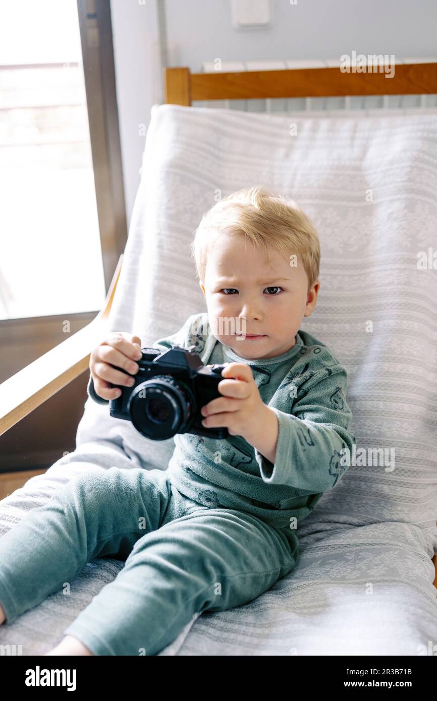 Baby boy sitting with camera on chair at home Stock Photo - Alamy