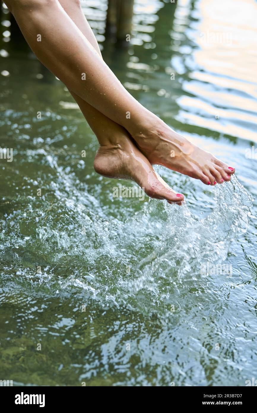 Woman splashing water with feet in lake Stock Photo - Alamy