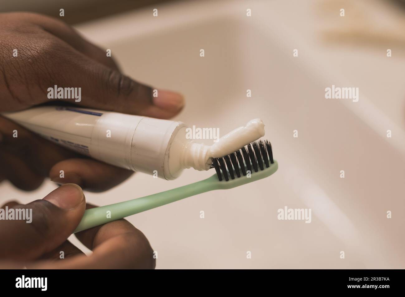 African american male hand holding toothbrush with toothpaste applied on it in bathroom. Close ...