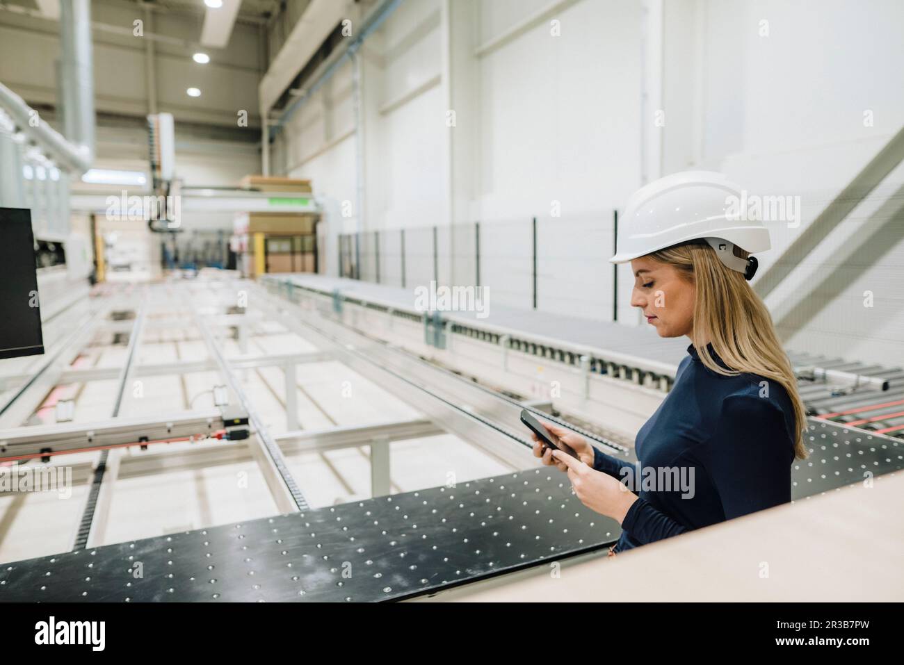 Businesswoman using smart phone standing in production hall at factory ...
